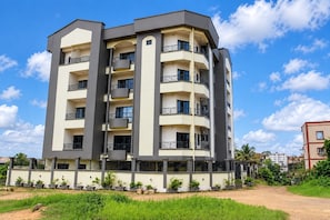 Um edifício residencial com vários andares, varandas, um telhado plano e um jardim ao redor.