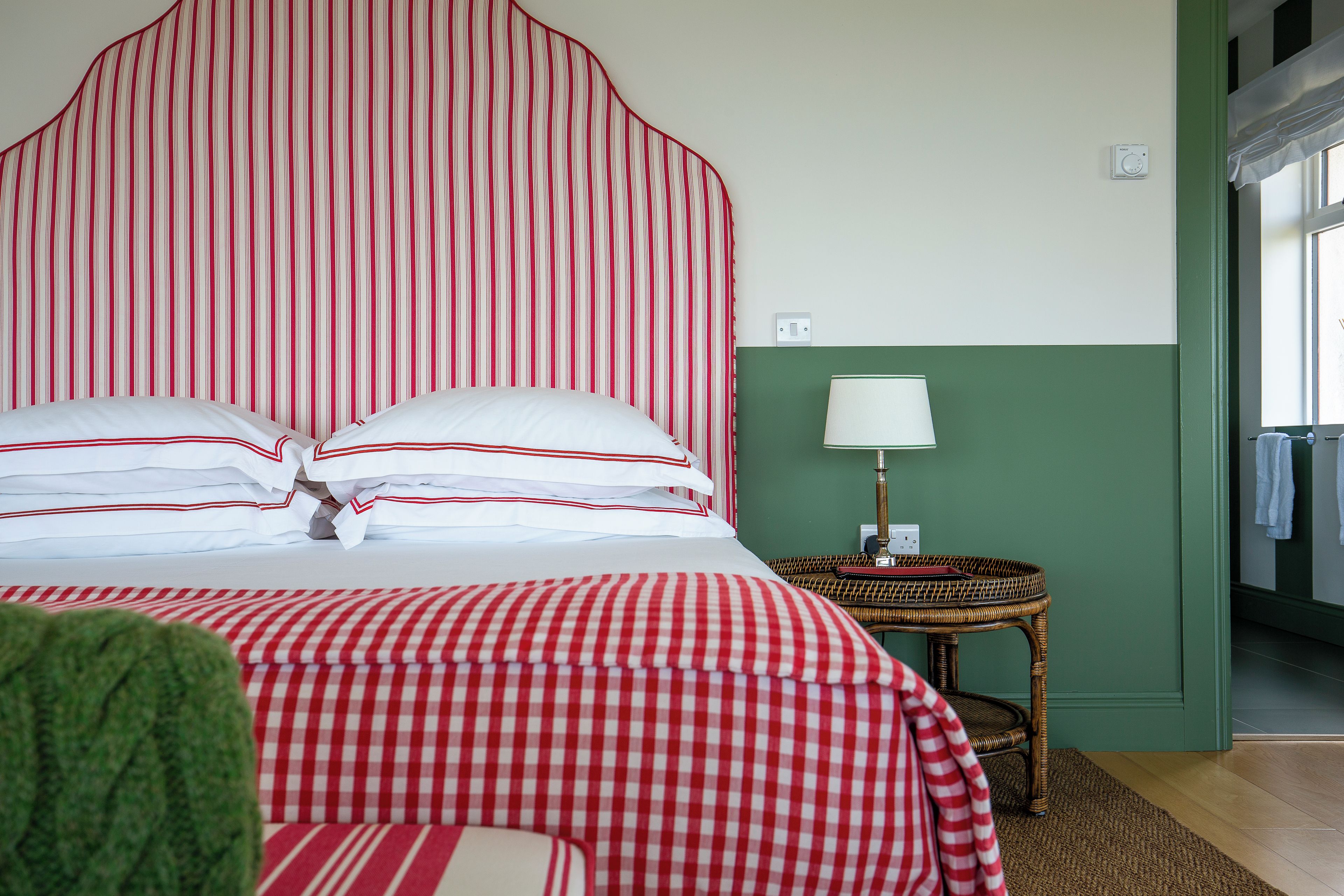 Uma cama com cabeceira listrada, uma mesa de cabeceira com abajur e uma parede verde.