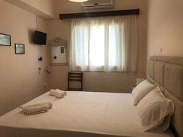Quarto de hotel com cama, cadeira, televisão, espelho e janela com cortinas.