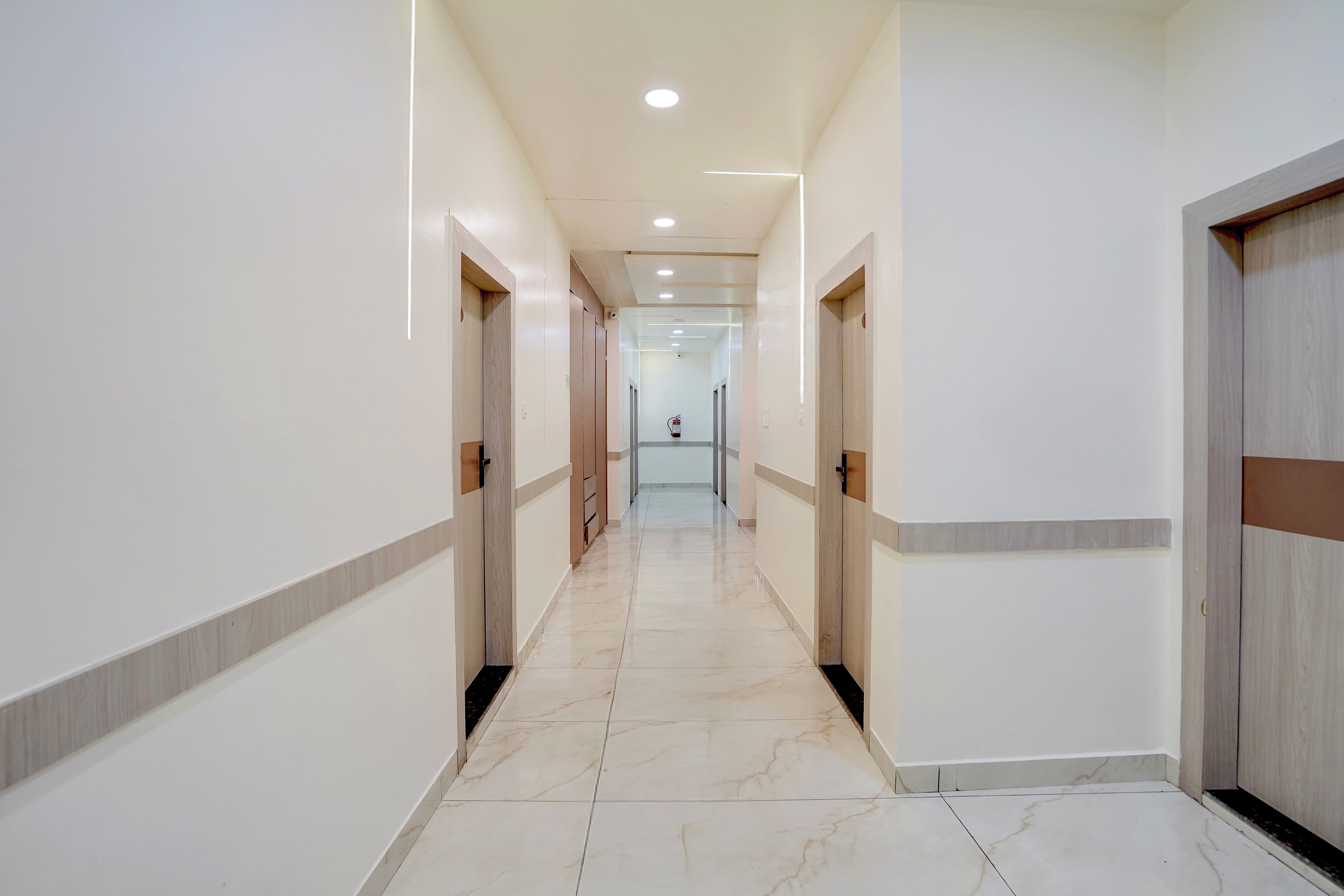 Um corredor com portas em ambos os lados, piso ladrilhado e iluminação embutida no teto.