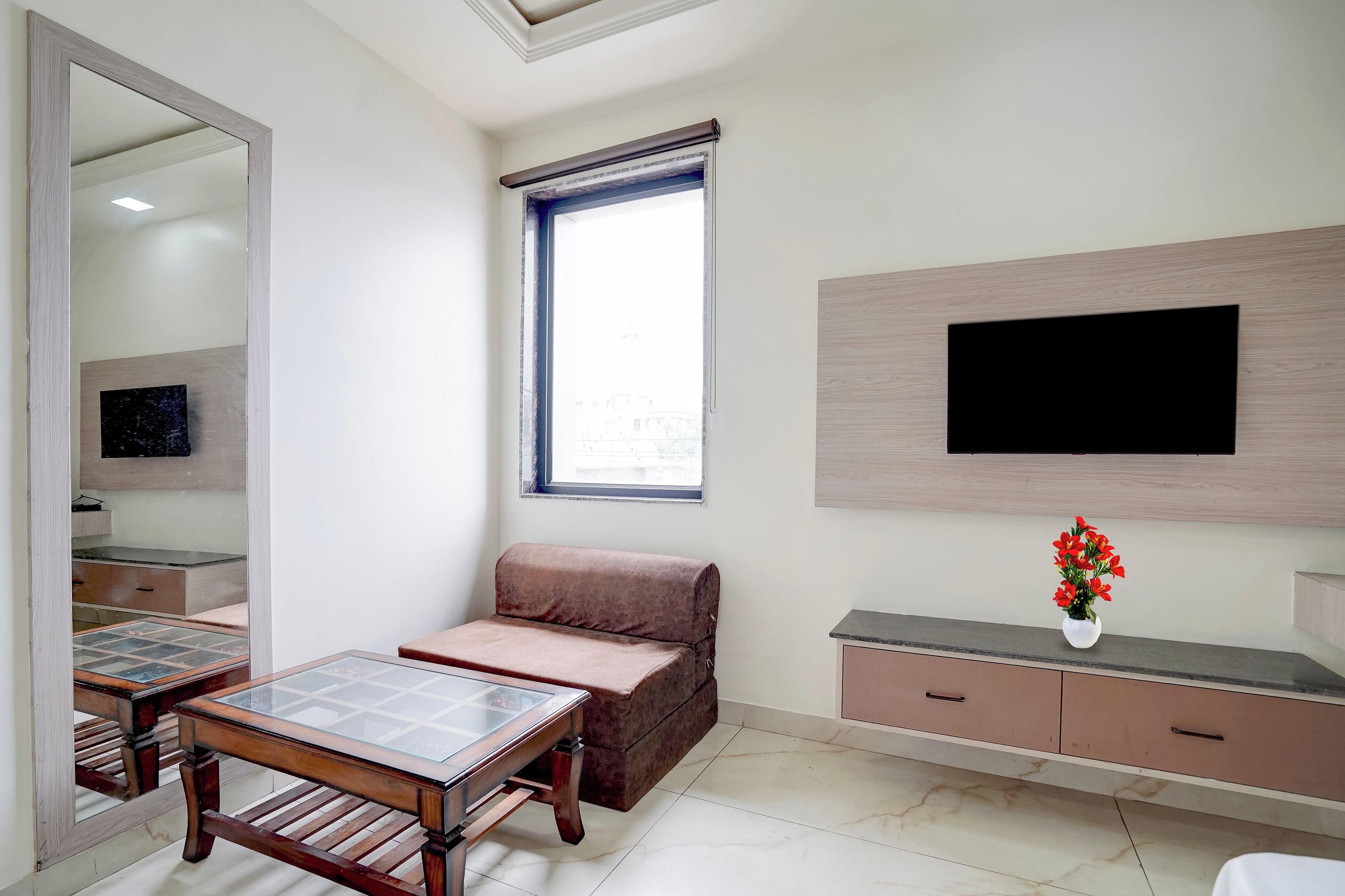 Uma sala de estar moderna com uma mesa de centro de vidro, um banco acolchoado, uma TV de tela plana na parede e um pequeno vaso de planta.