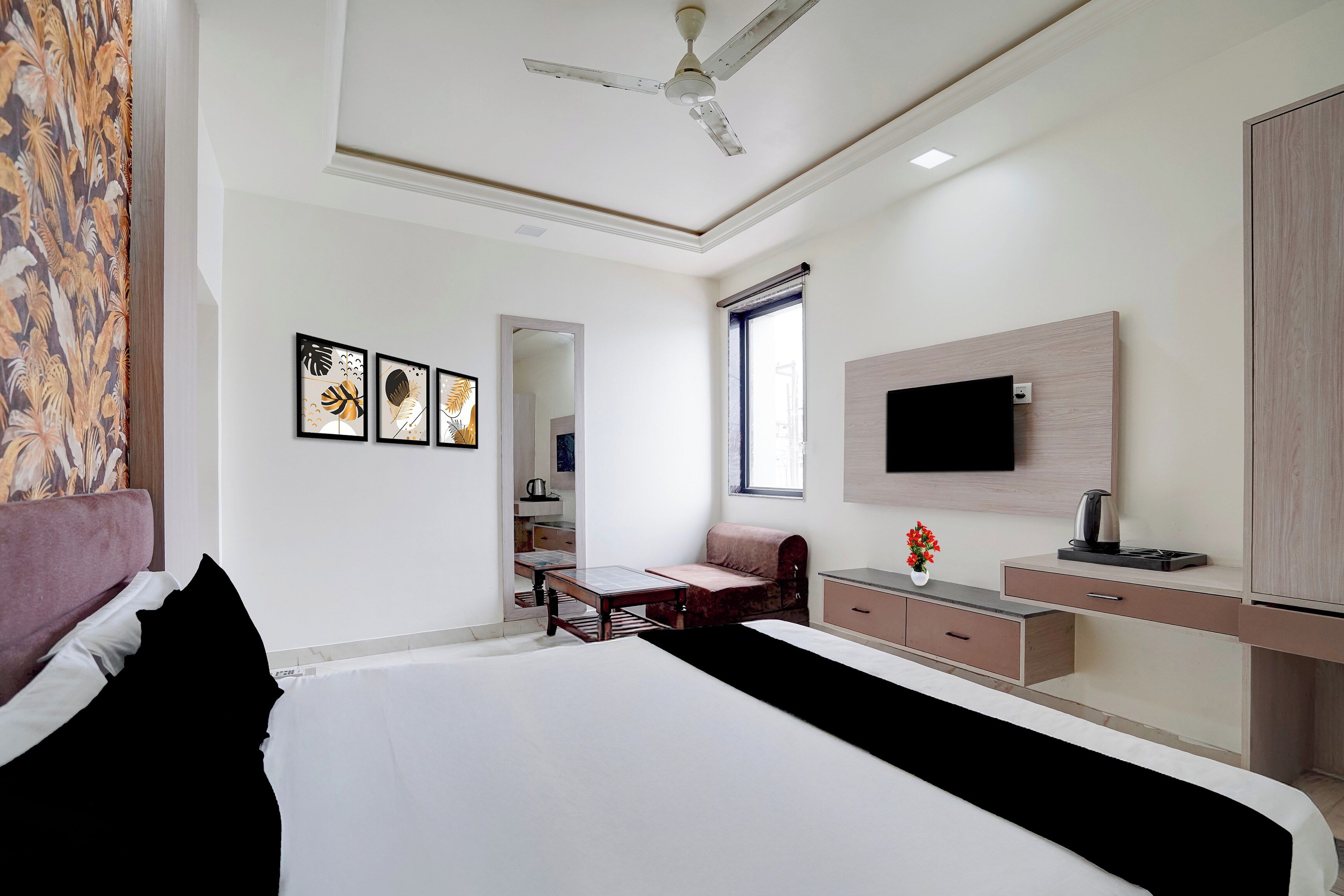 Quarto de hotel com cama, escrivaninha, cadeira, televisão e ventoinha no teto.