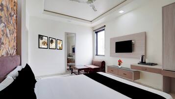 Quarto de hotel com cama, escrivaninha, cadeira, televisão e ventoinha no teto.