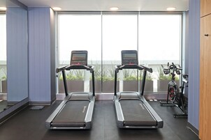 Academia com duas esteiras, uma bicicleta ergométrica e uma janela com vista para o verde.