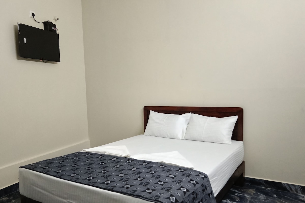 Uma cama de solteiro com cabeceira de madeira, colchão branco e edredom estampado.