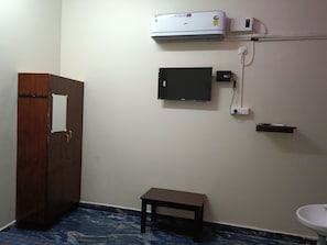 Quarto com porta de madeira, uma mesa pequena, ar-condicionado fixado na parede, televisão e pia.