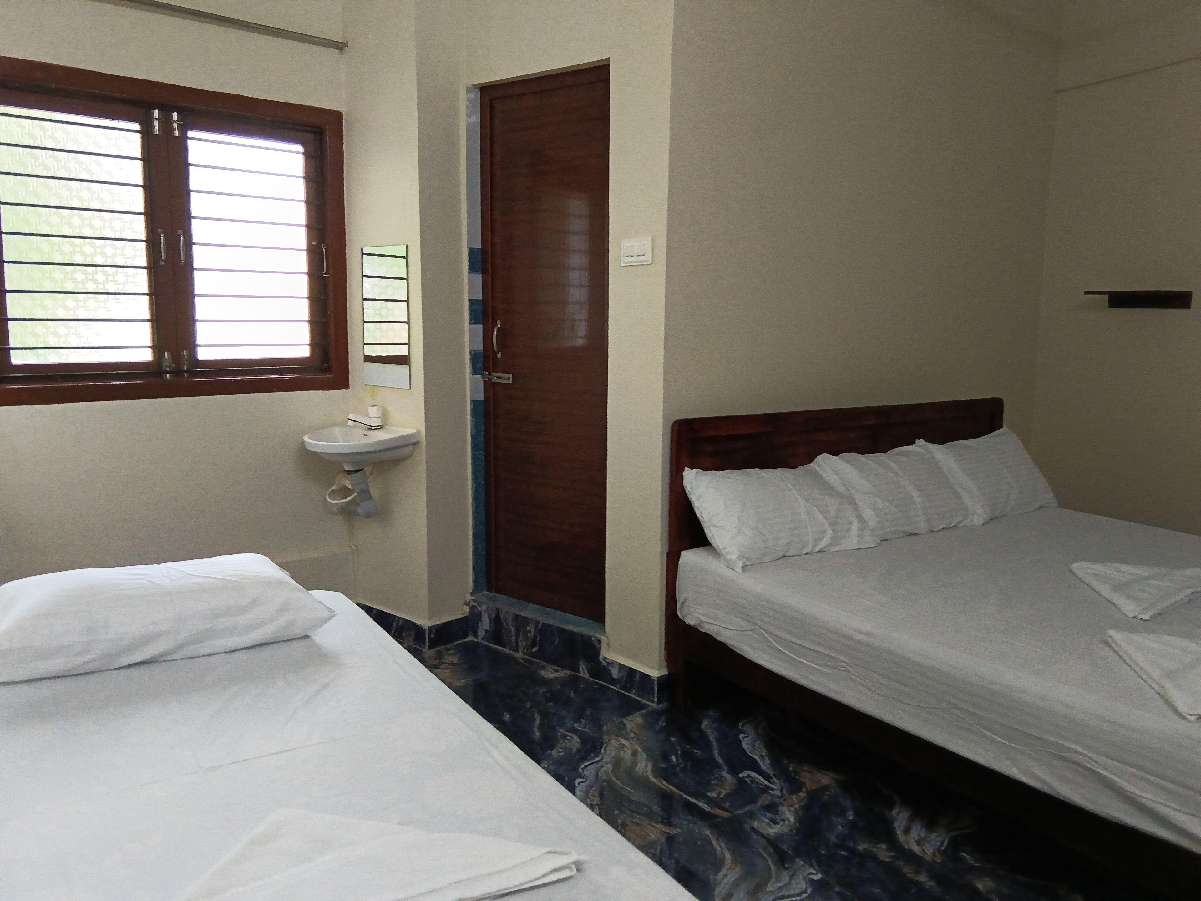 Quarto com duas camas, porta de madeira, janela com persianas e pia.