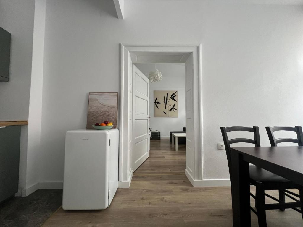 Cozinha moderna com geladeira branca, piso de madeira e área de jantar com mesa e cadeiras escuras.