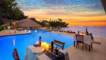 Mesa de jantar posta com velas, piscina e vista para o pôr do sol.