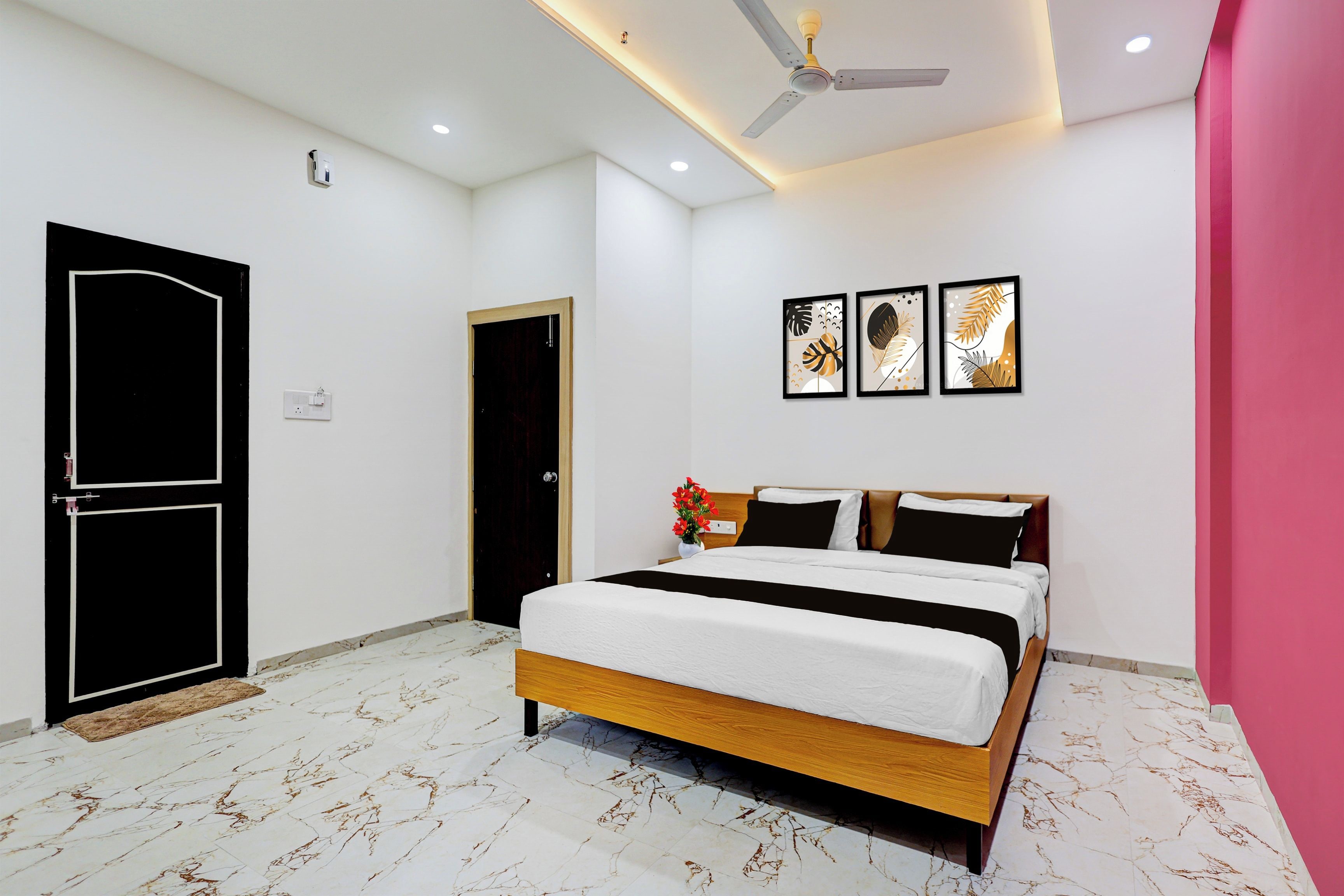 Quarto de hotel com cama, ventoinha no teto, porta e três obras de arte emolduradas na parede.