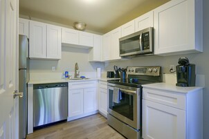 Cozinha moderna com eletrodomésticos de aço inoxidável, armários brancos e piso de madeira.