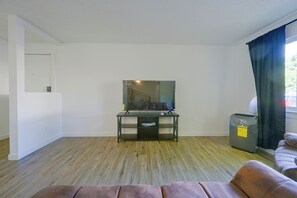 Quarto com piso de madeira, uma escrivaninha cinza com espelho, um sofá marrom e uma janela com cortina.