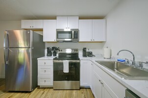 Cozinha moderna com eletrodomésticos de aço inoxidável, armários brancos e bancada de mármore.