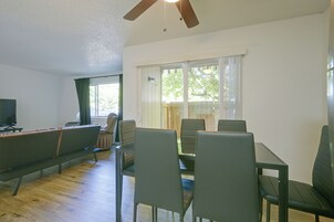 Um quarto com mesa de jantar, cadeiras, sofá, televisão e ventoinha no teto.