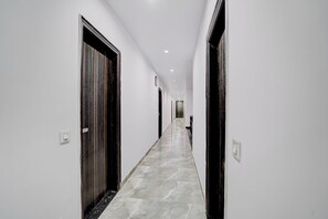 Um corredor com paredes brancas, portas de madeira escura e chão de mármore.