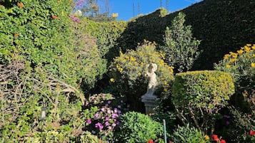 Um jardim com uma estátua, diversas plantas e um caminho de tijolos.