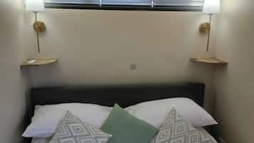 Cama com almofadas estampadas, cabeceira e duas luminárias de cabeceira.
