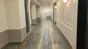 Um corredor longo e bem iluminado, com piso lustroso, portas em ambos os lados e iluminação embutida no teto.