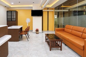 Uma área de recepção moderna com sofá, mesa de centro, televisão e balcão com cadeiras.