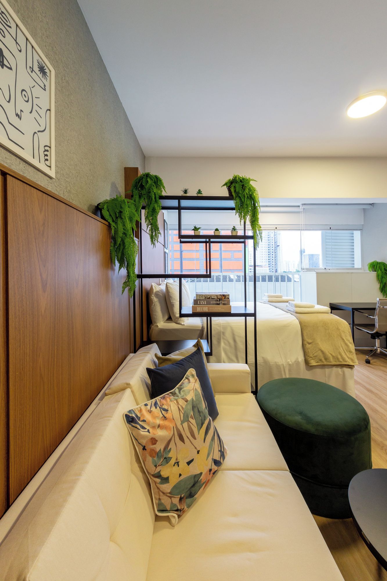 Sala de estar moderna com um sofá, uma mesinha e um banco. Há plantas na parede e uma janela com vista para edifícios.