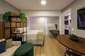 Quarto de hotel moderno com uma cama, área de estar com uma mesa, escrivaninha e estante de livros.