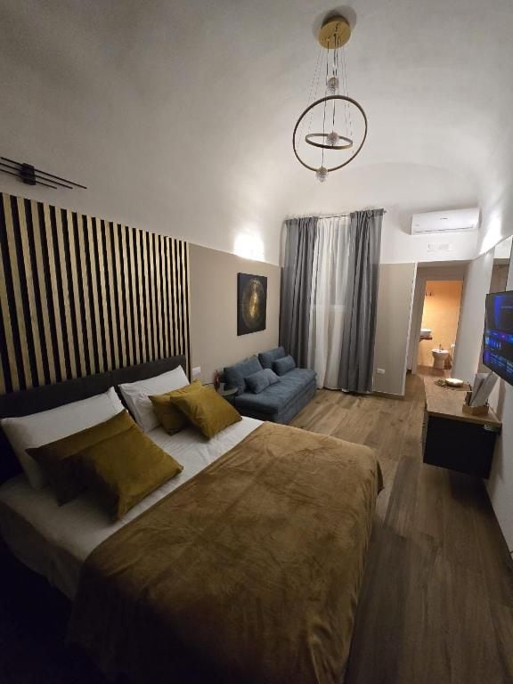 Quarto de hotel com cama, sofá, televisão e banheiro visível por uma porta aberta.