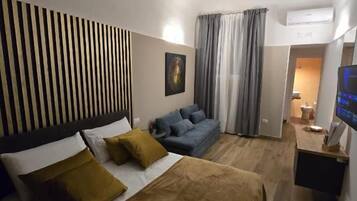 Quarto de hotel com cama, sofá, televisão e banheiro visível por uma porta aberta.