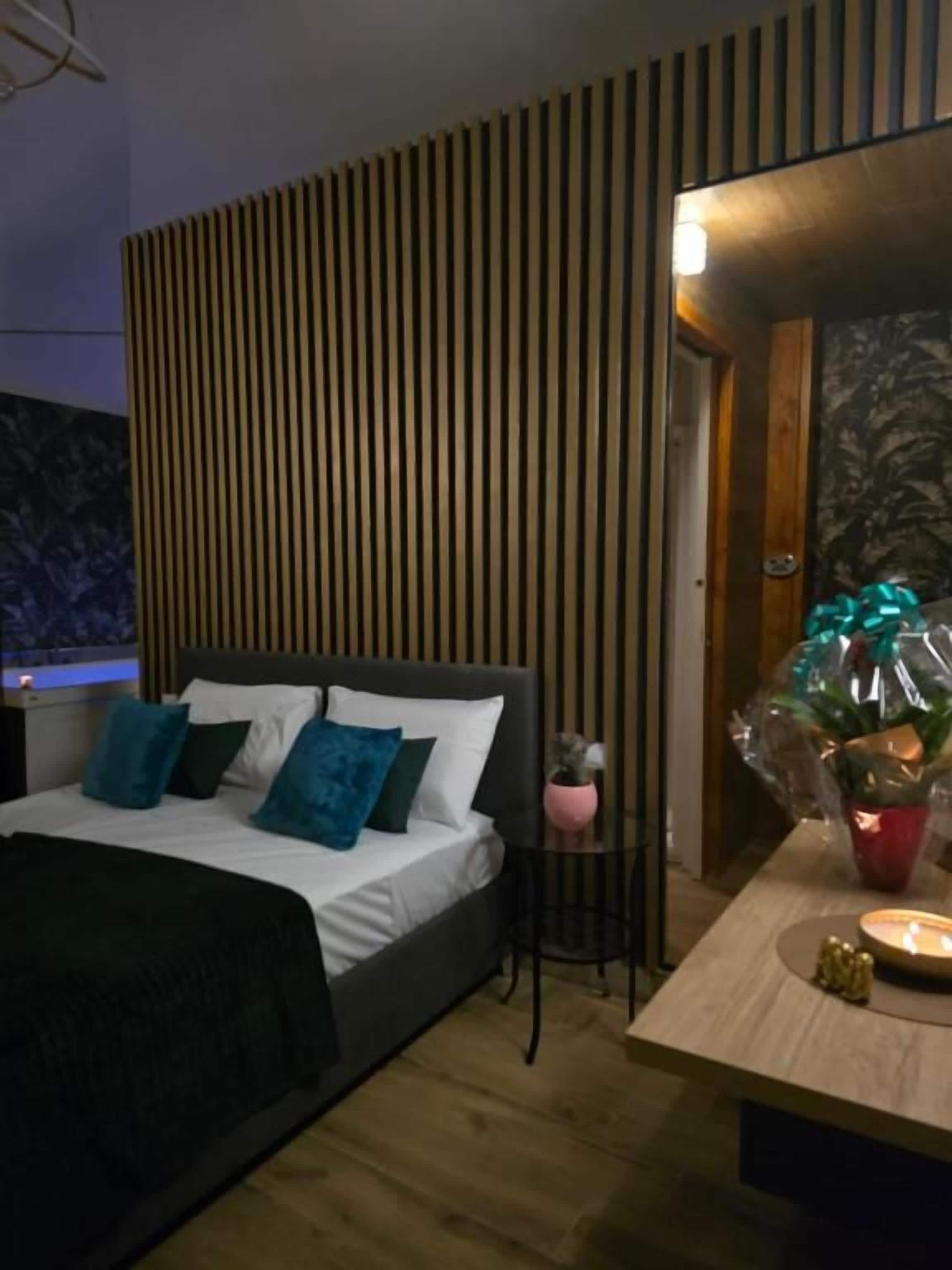 Quarto com cama, mesa de cabeceira e luminária na parede.