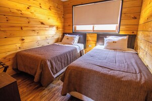 Uma cabana com duas camas de madeira, cada uma com encosto e travesseiro, e uma janela acima.