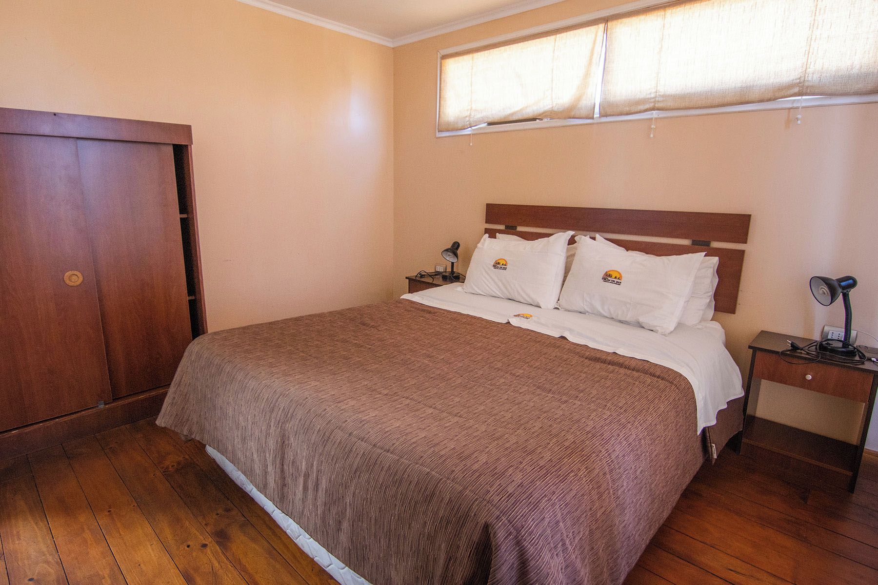Quarto com cama, mesa de cabeceira, luminária, guarda-roupa e janela com cortinas.