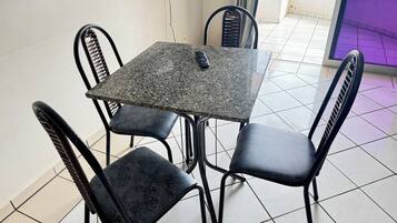 Mesa quadrada com controle remoto, rodeada por quatro cadeiras com padrão de folha.