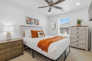 Quarto com cama, mesa de cabeceira, cômoda, ventilador de teto e obras de arte na parede.