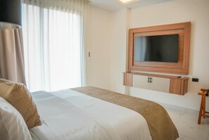 Quarto de hotel com cama, televisão presa à parede e janela com cortinas.