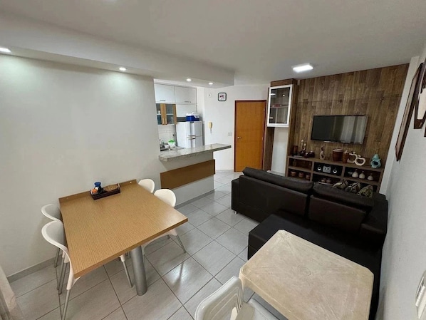 Um espaço de estar moderno, com área de jantar, conjunto de sofás e cozinha ao fundo.