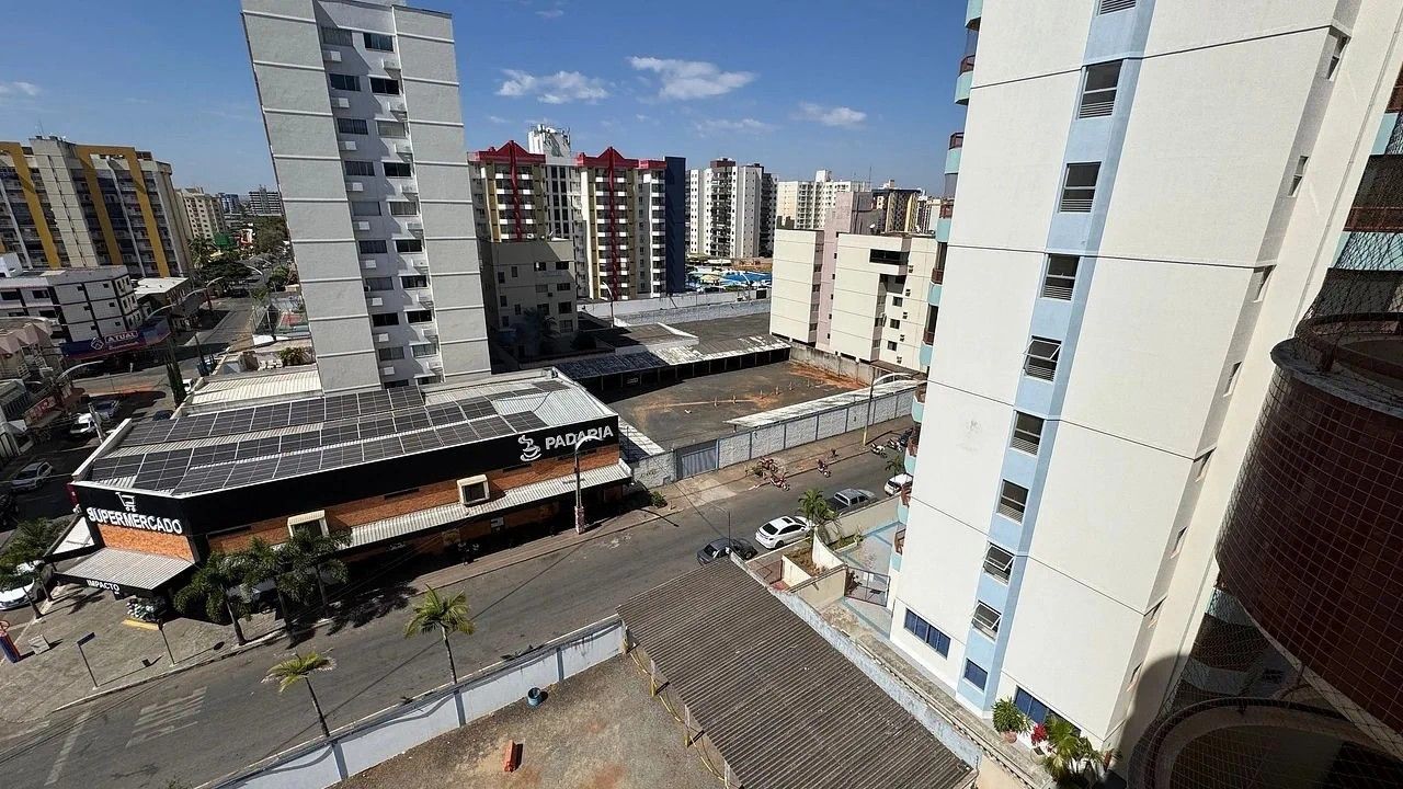 Edifício de vários andares com um telhado coberto de painéis solares, cercado por outros edifícios altos.