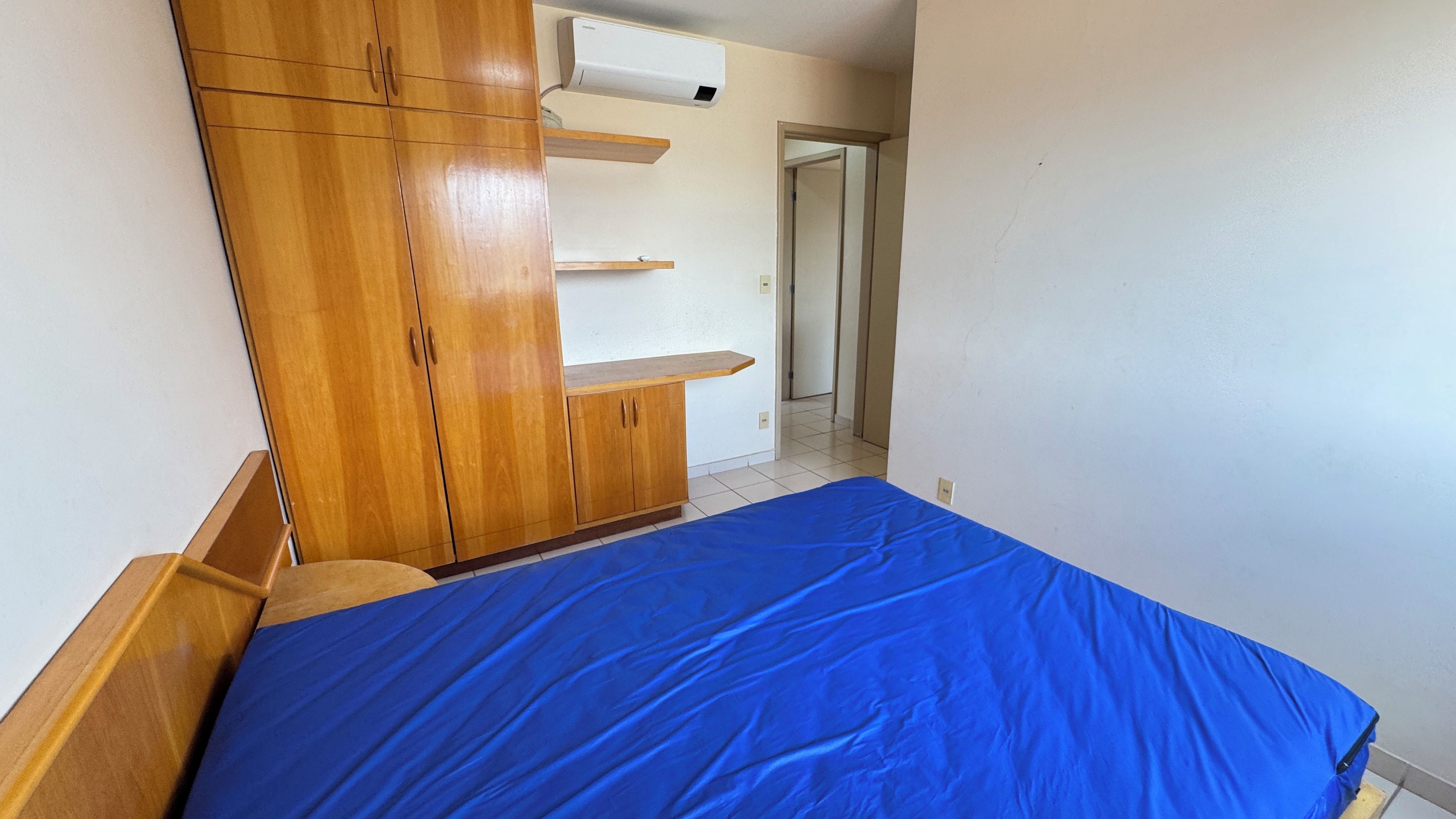 Quarto com cama, guarda-roupa de madeira e parede branca.