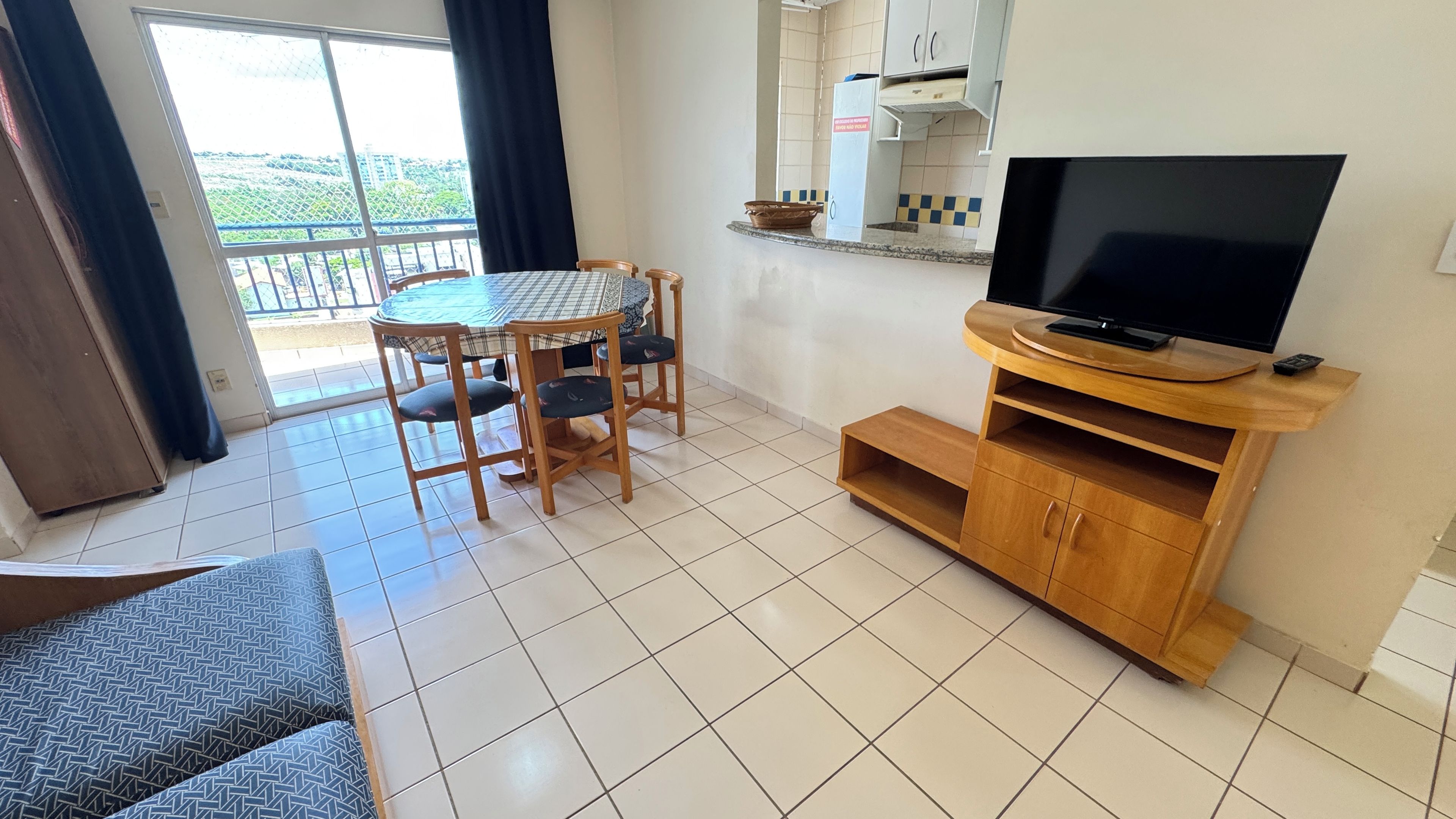 Sala de estar com televisão, móvel de entretenimento em madeira, mesa de jantar e cadeiras.