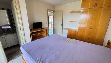 Quarto com cama, televisão, guarda-roupa de madeira e pequena escrivaninha.