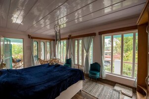 Quarto com cama grande, varanda com cadeiras e várias janelas.