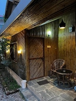 Fachada de madeira com parede de bambu, porta de vidro e área de estar com cadeiras de vime e uma mesa.