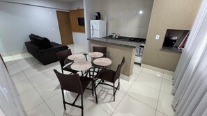 Cozinha moderna com área de jantar, incluindo mesa de vidro, cadeiras de vime e um sofá preto.