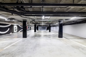 Garagem de estacionamento com pisos de concreto, pilares pretos e tubulações no teto.