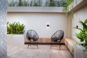 Área de estar moderna ao ar livre, com duas cadeiras, luminária e plantas.