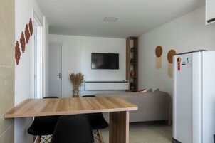 Cozinha moderna com mesa de madeira, cadeiras pretas, TV embutida e geladeira branca.
