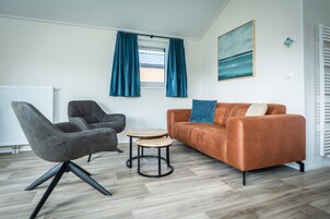 Uma sala de estar moderna com uma poltrona cinza, um sofá marrom e duas mesas redondas de madeira.