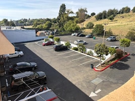 Um parque de estacionamento com vários carros, árvores e um edifício ao fundo.