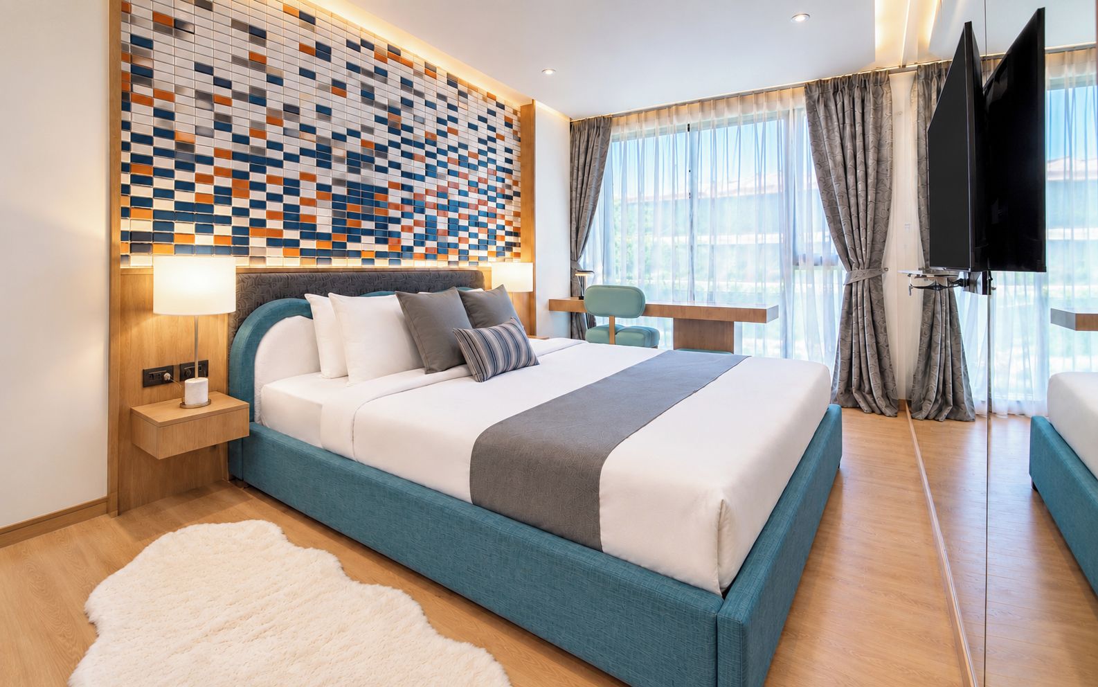 Quarto de hotel moderno com uma cama grande, uma escrivaninha, uma cadeira, uma televisão e uma parede com padrão.