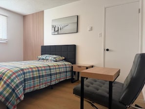 Um quarto com cama, cadeira, escrivaninha e porta.