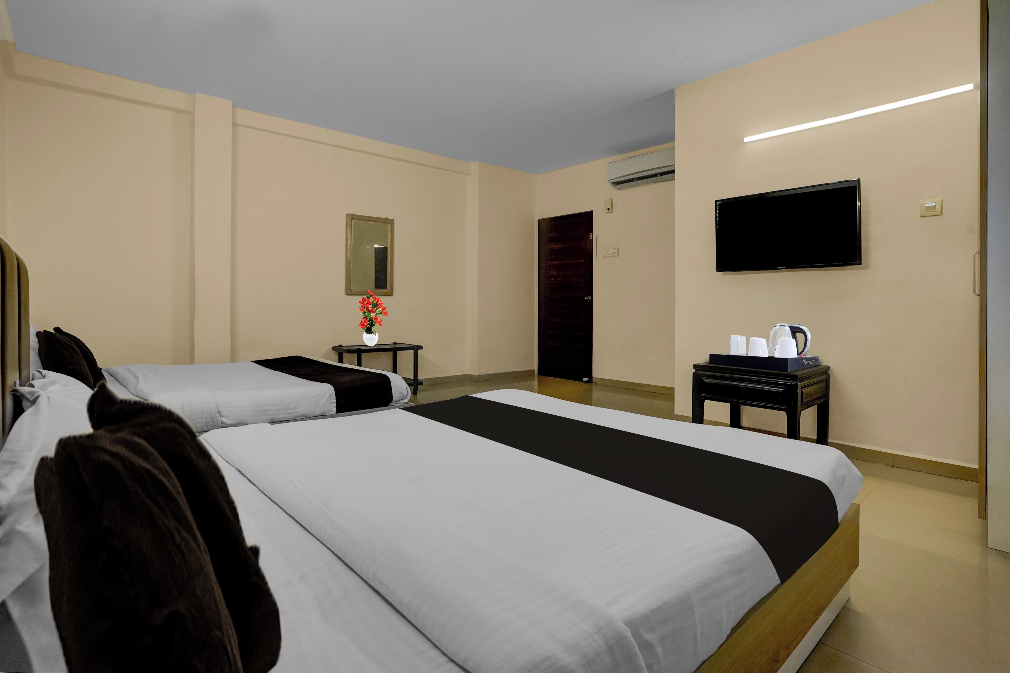 Quarto de hotel com duas camas, uma TV de tela plana, uma mesinha com um vaso de flores e uma cafeteira.