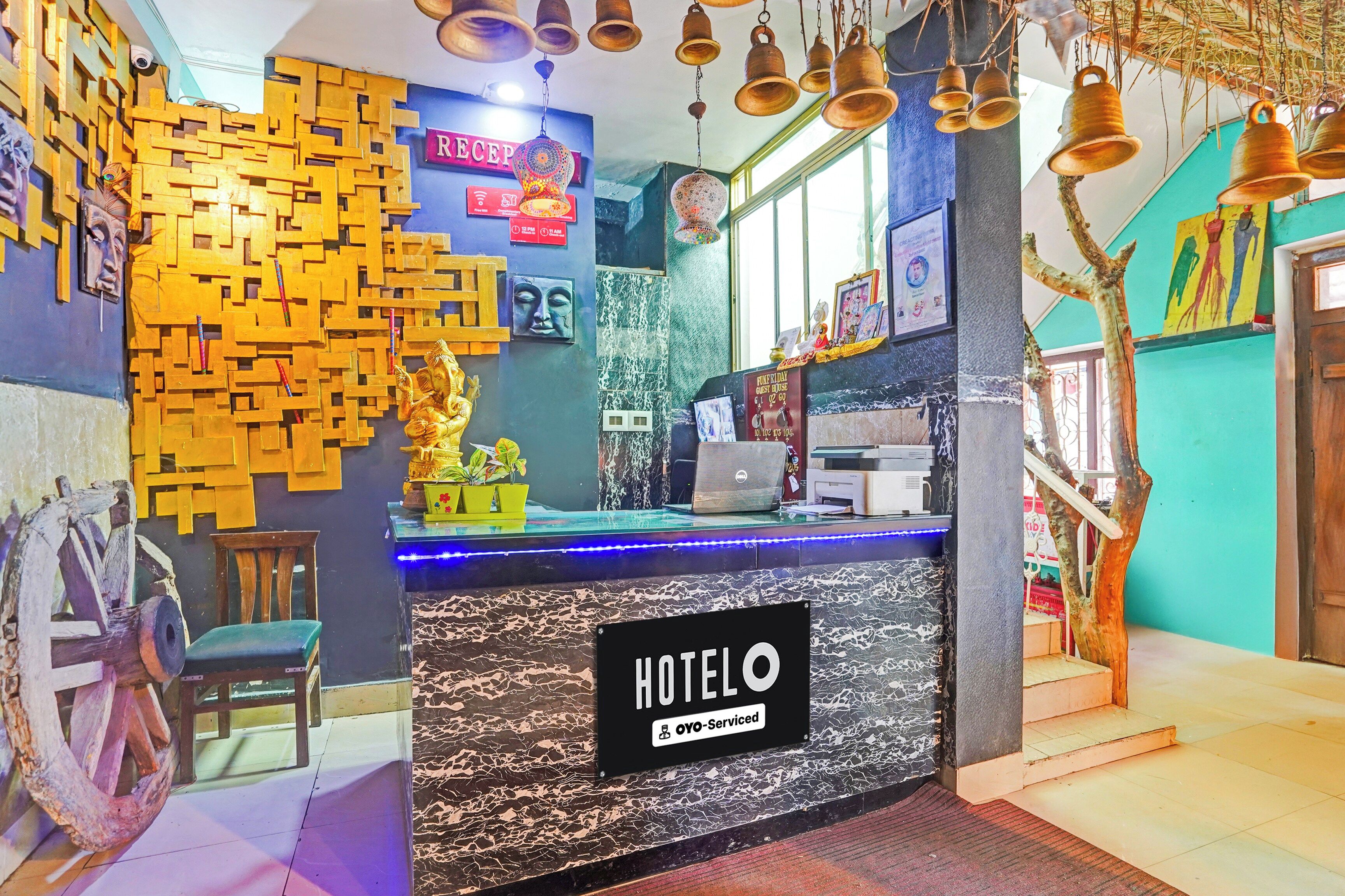 Bancada de recepção de hotel com uma placa indicando 'HOTEL OYO-Serviced', decoração de parede em madeira e área de recepção com computador e planta.
